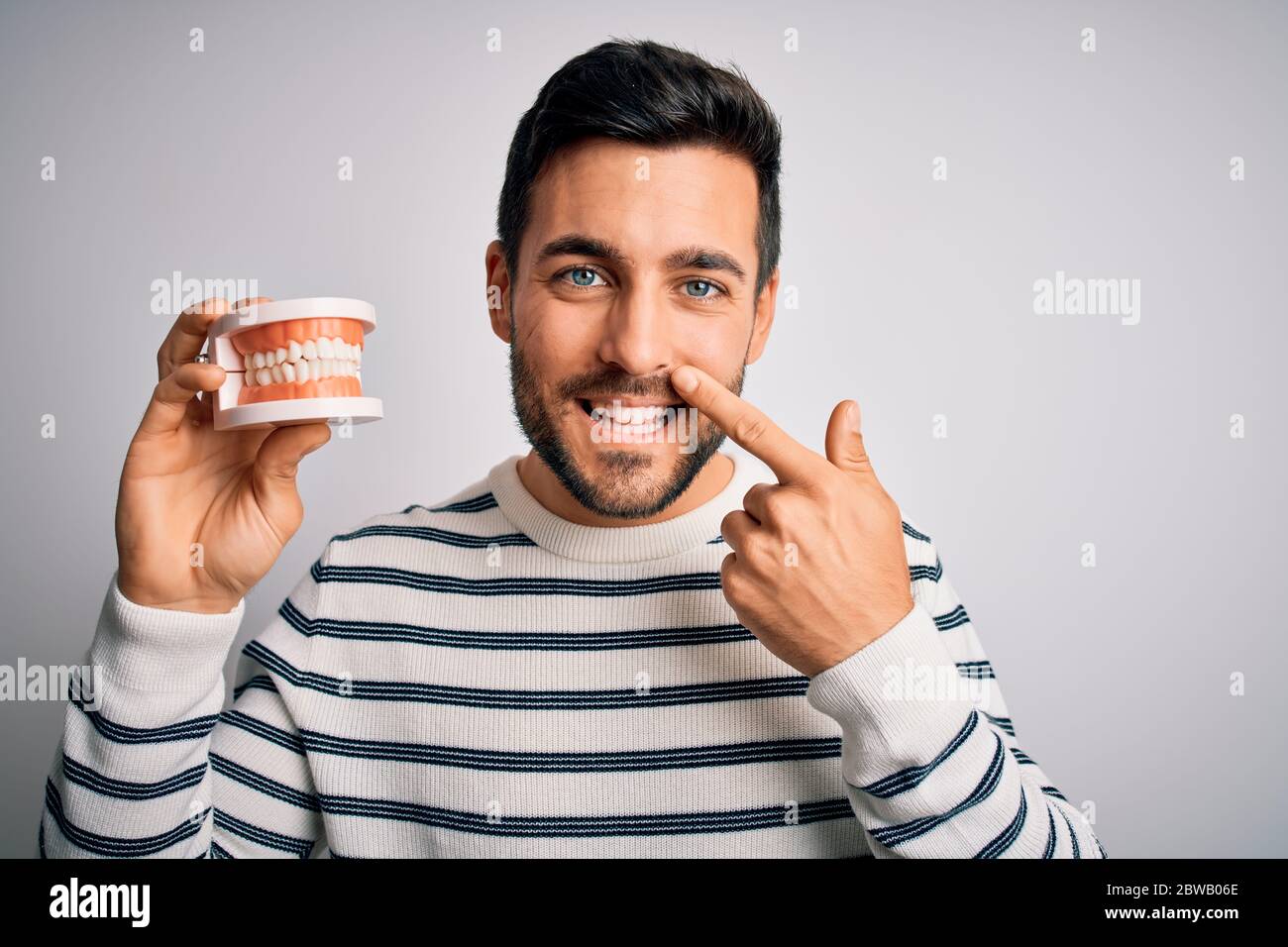 Young handsome man with beard holding plastic denture teeth over white ...