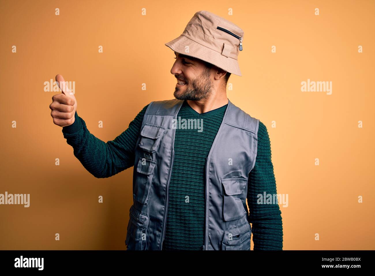 Handsome tourist man with beard on vacation wearing explorer hat over ...