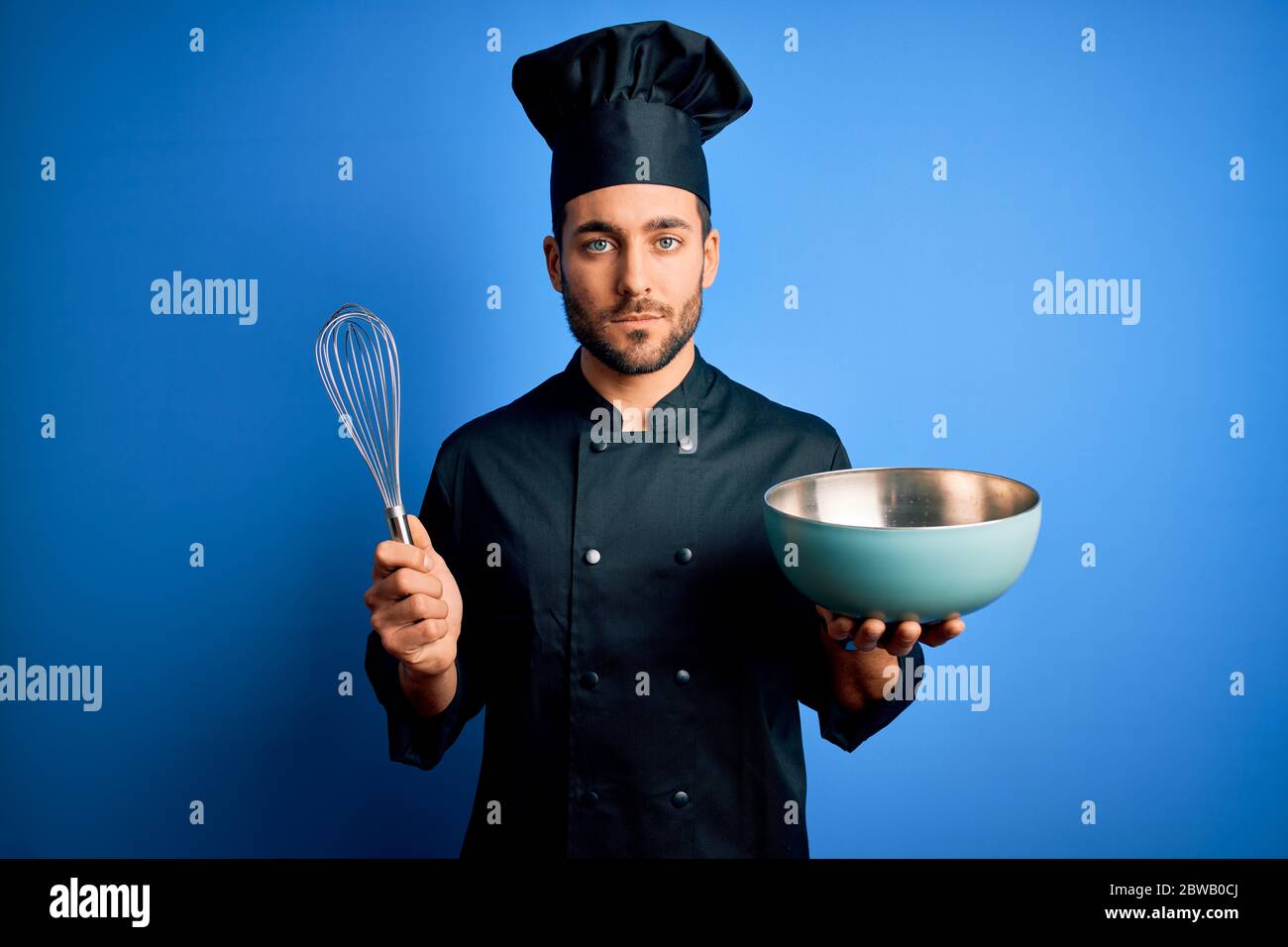 Young cooker man with beard wearing uniform using whisk and bowl over ...