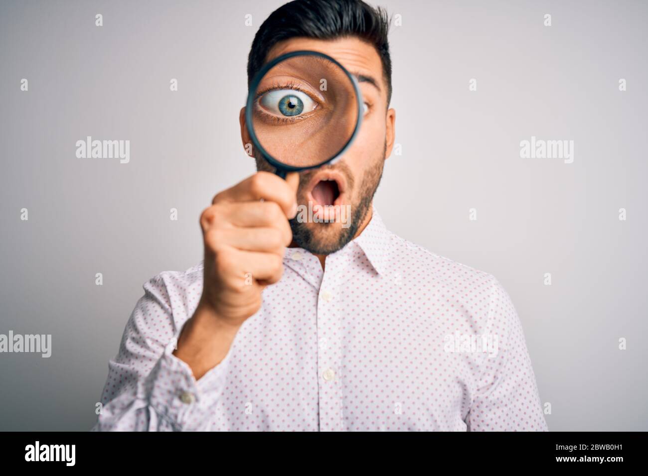 Young detective man looking through magnifying glass over isolated ...