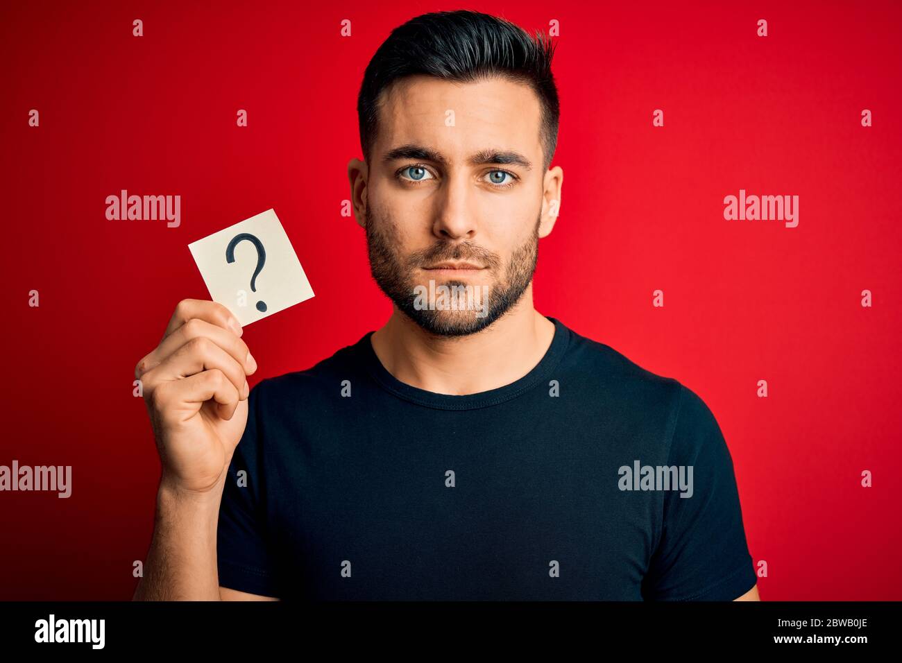 Young handsome man holding paper with question mark symbol over red ...