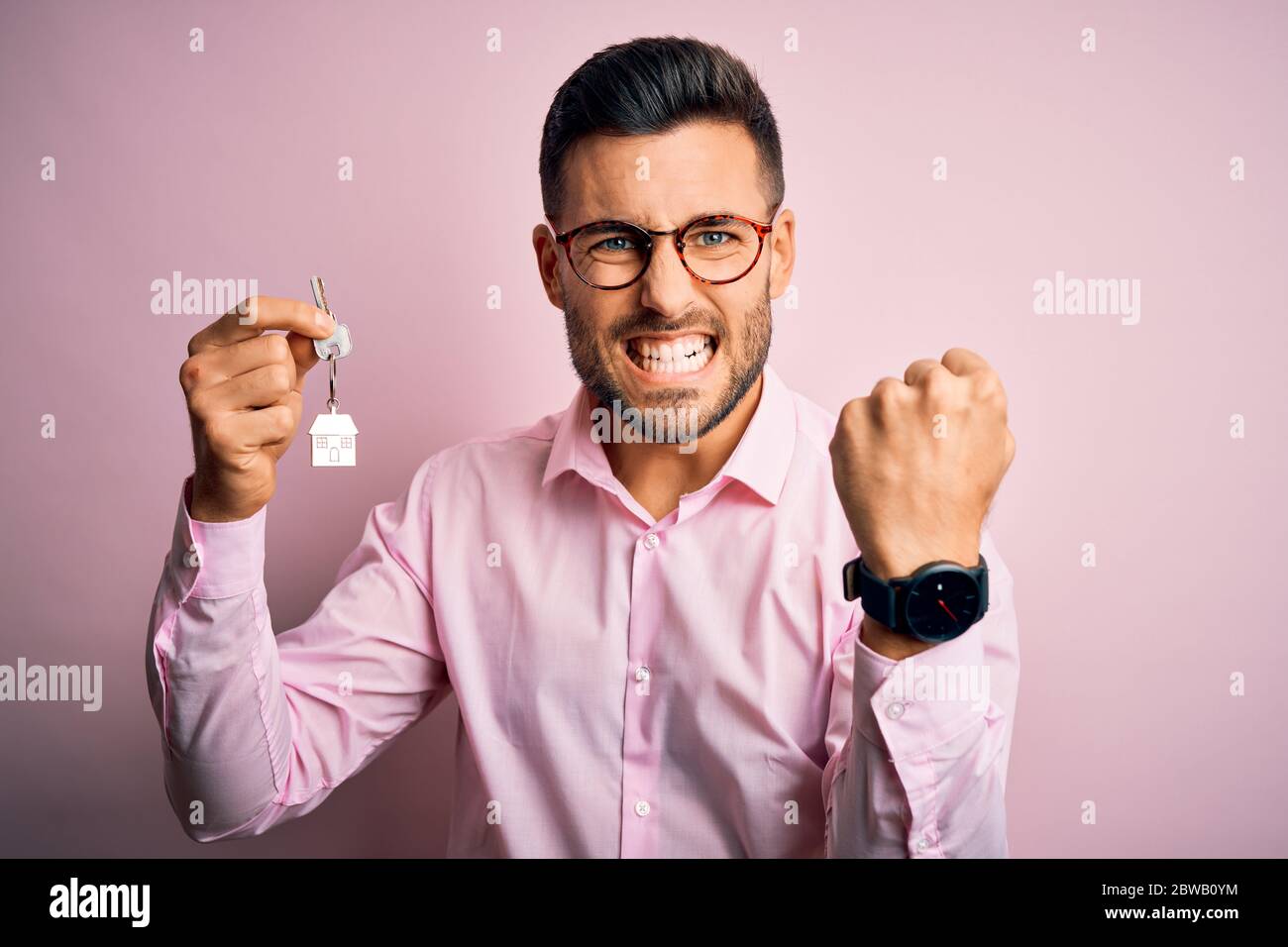 Young real estate business man holding new house keys over pink ...