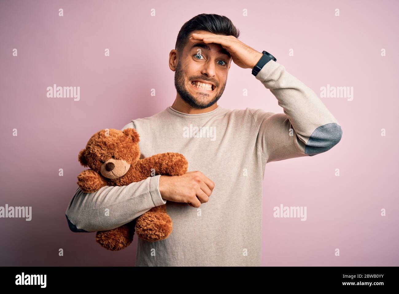 Young handsome man holding teddy bear standing over isolated pink ...