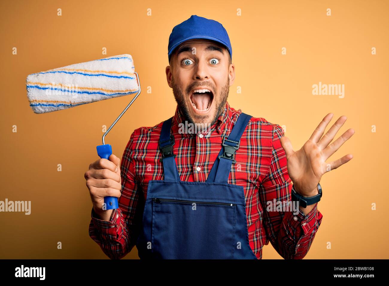 Young handsome painter man painting wall using roller over isolated ...