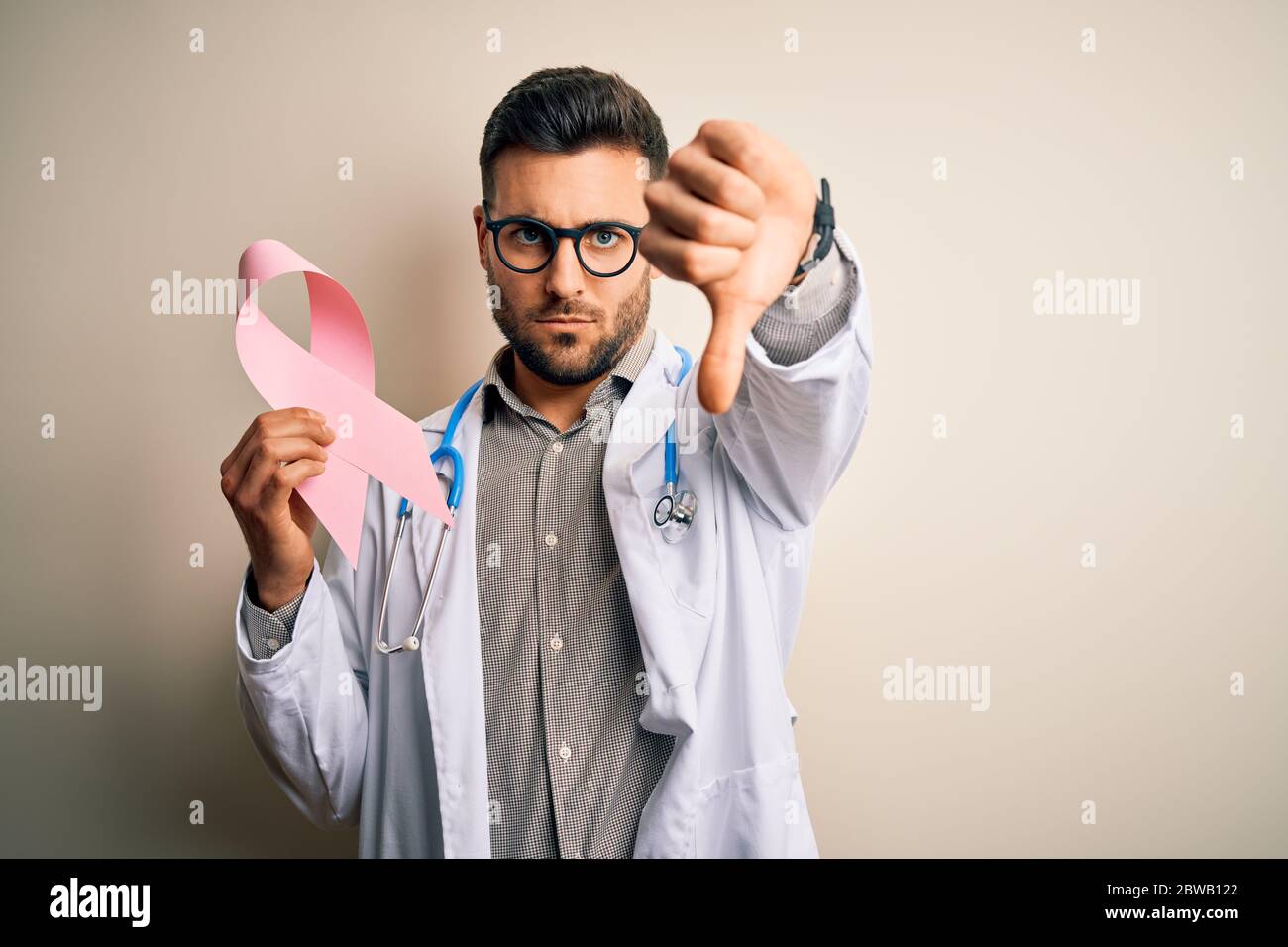 Young doctor man wearing stethoscope holding pink ribbon about cancer ...