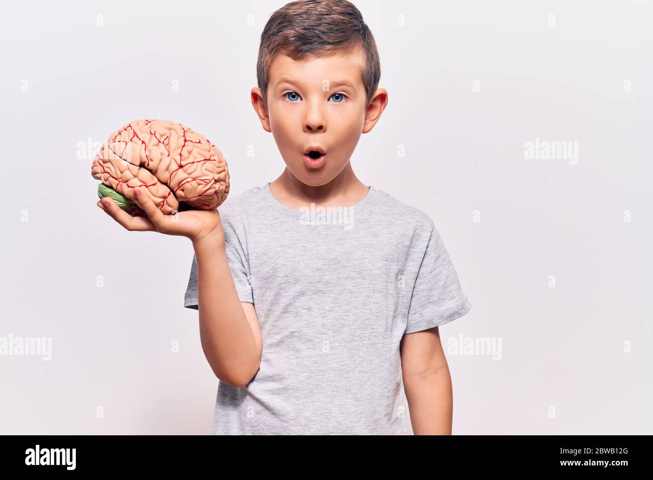 Cute blond kid holding brain scared and amazed with open mouth for ...