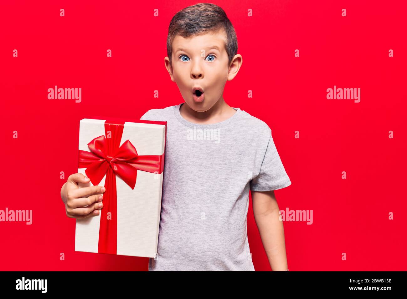 Cute blond kid holding gift scared and amazed with open mouth for ...