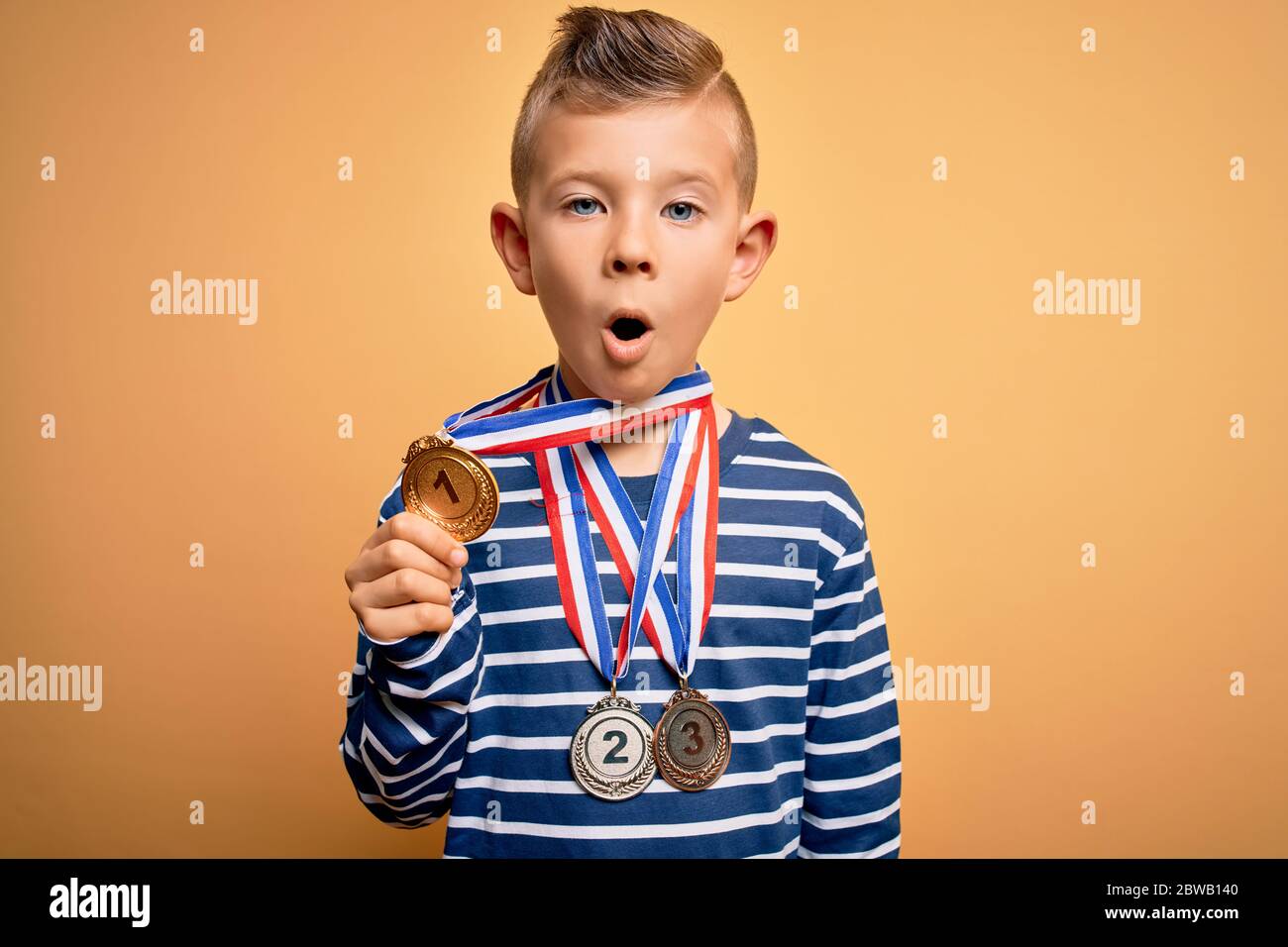 Young little caucasian winner kid wearing award competition medals over ...