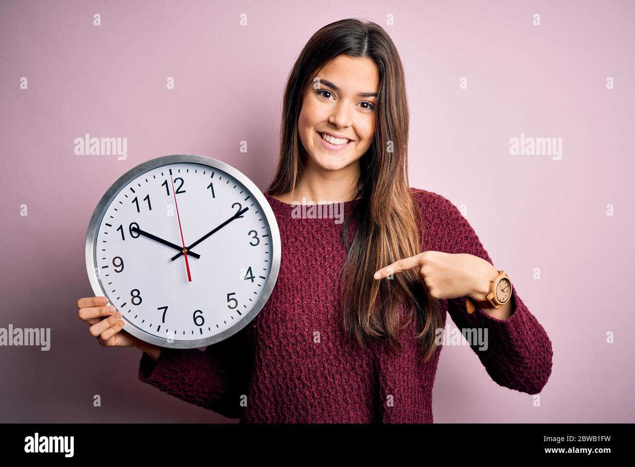 Young beautiful girl doing countdown holding big clock over isolated ...