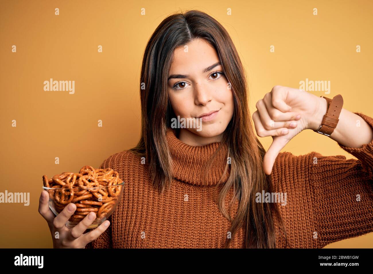 Young beautiful girl eating baked german pretzel standing over isolated ...