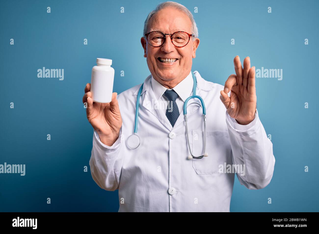 Senior grey haired doctor man holding pharmaceutical pills over blue ...