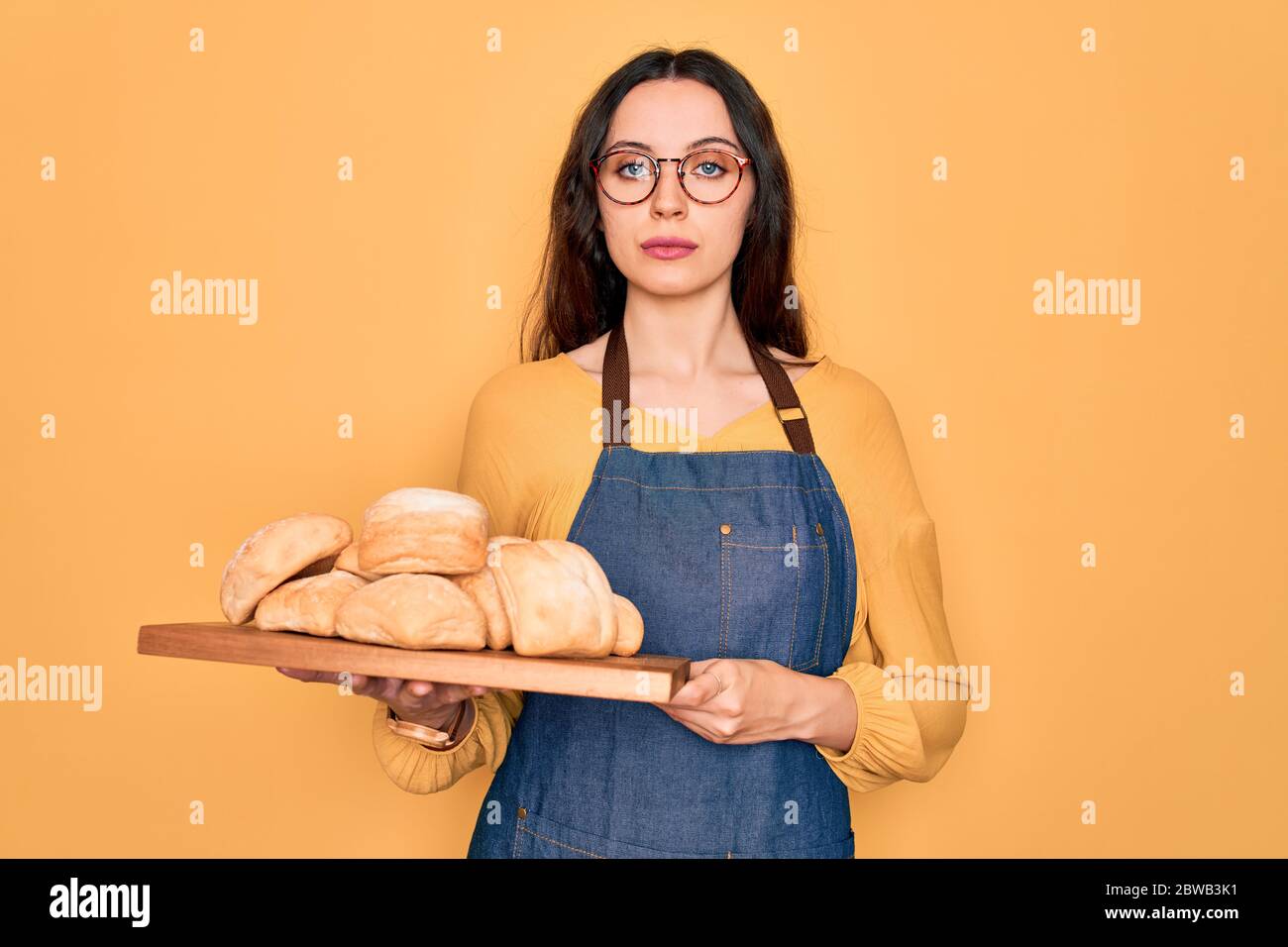 Young beautiful baker woman with blue eyes wearing apron holding tray ...