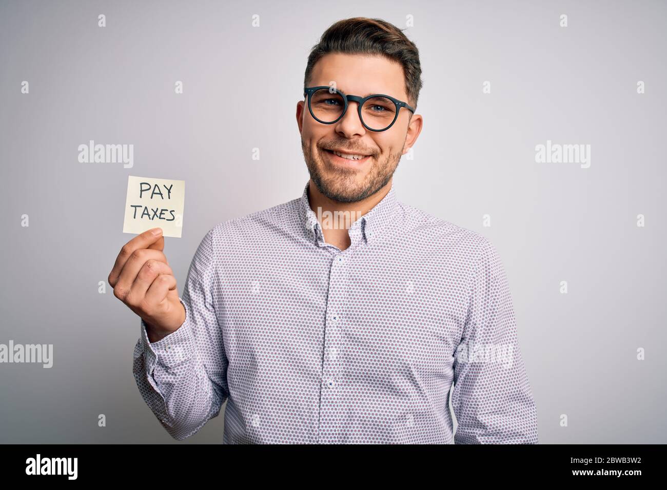Young business man with blue eyes holding pay taxes word on paper note ...