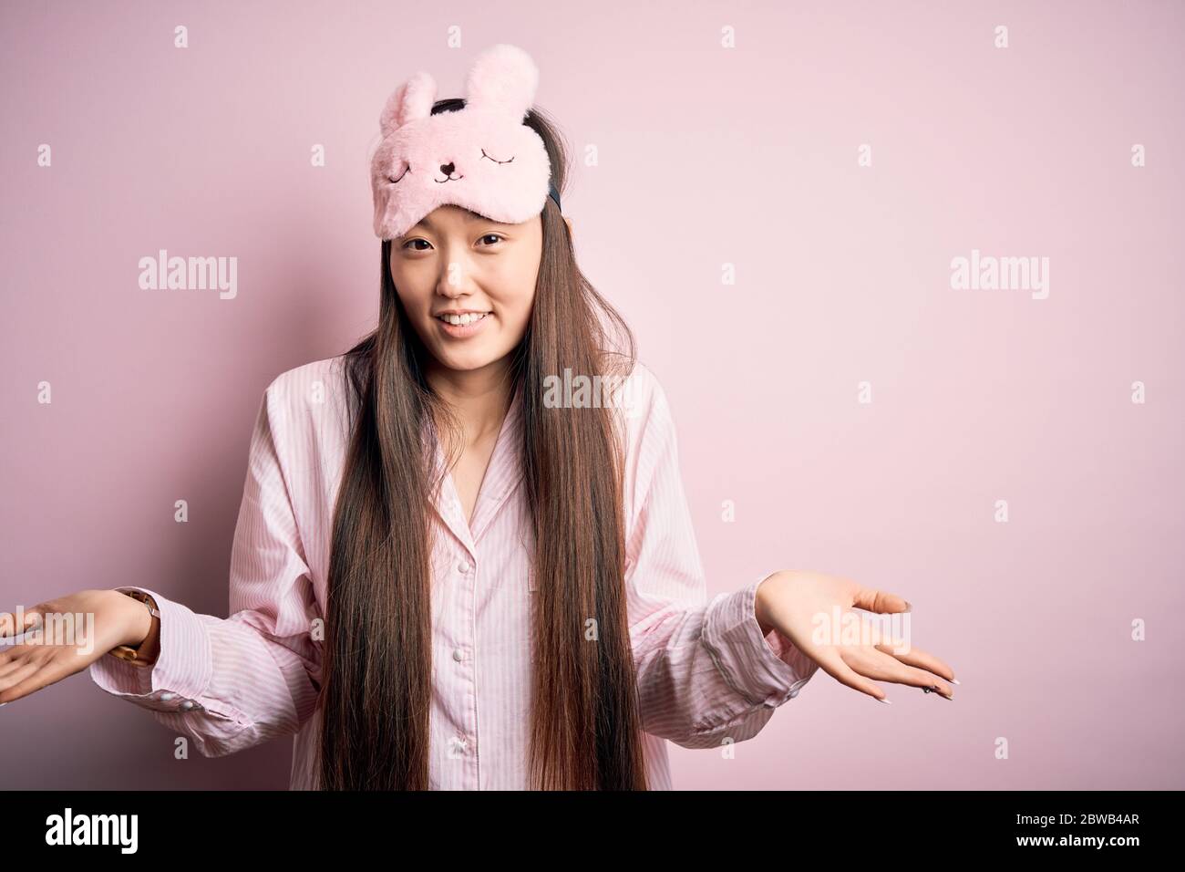 Young asian woman wearing pajama and sleep mask over pink isolated ...