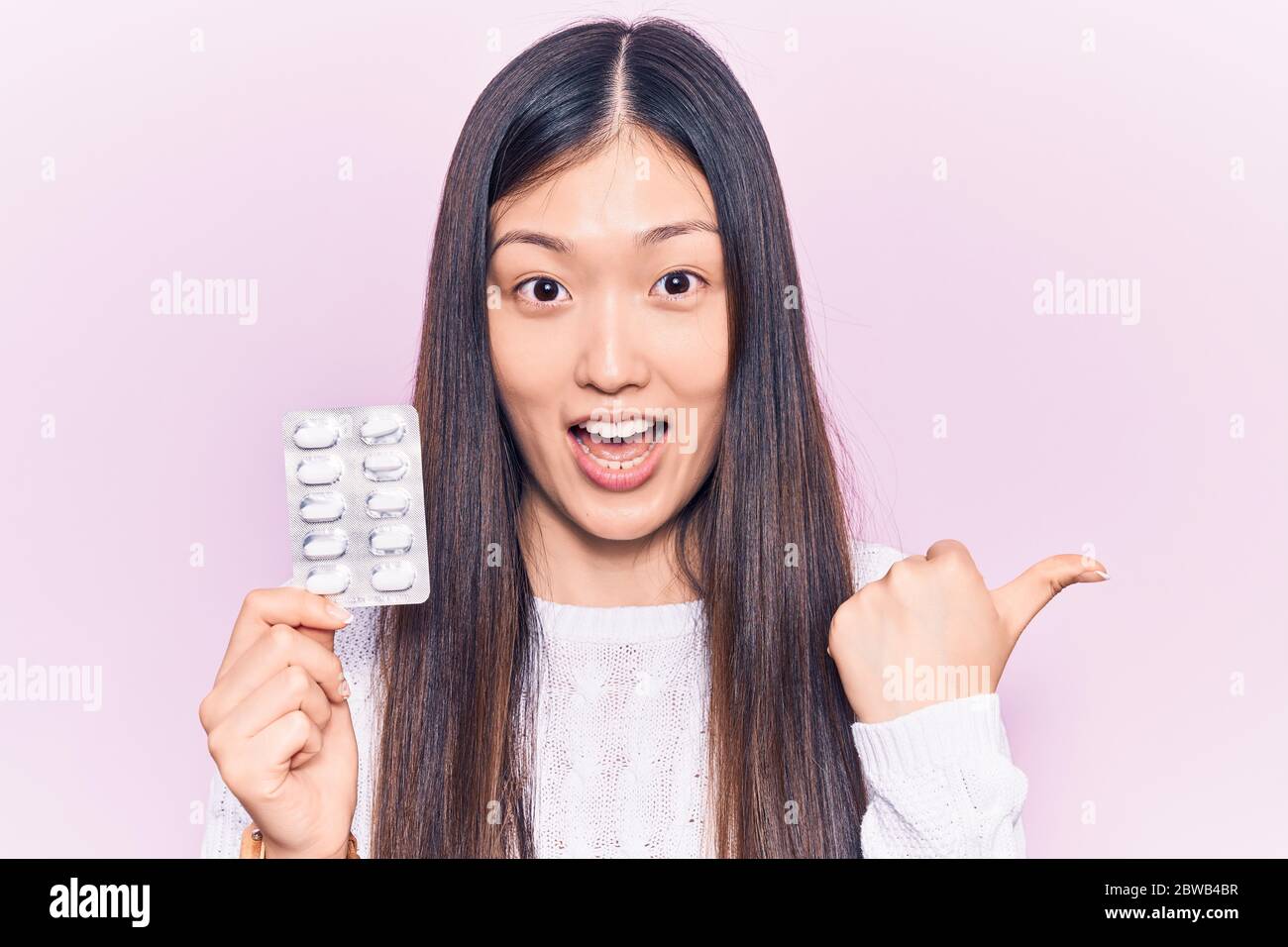 Young beautiful chinese woman holding pills pointing thumb up to the ...