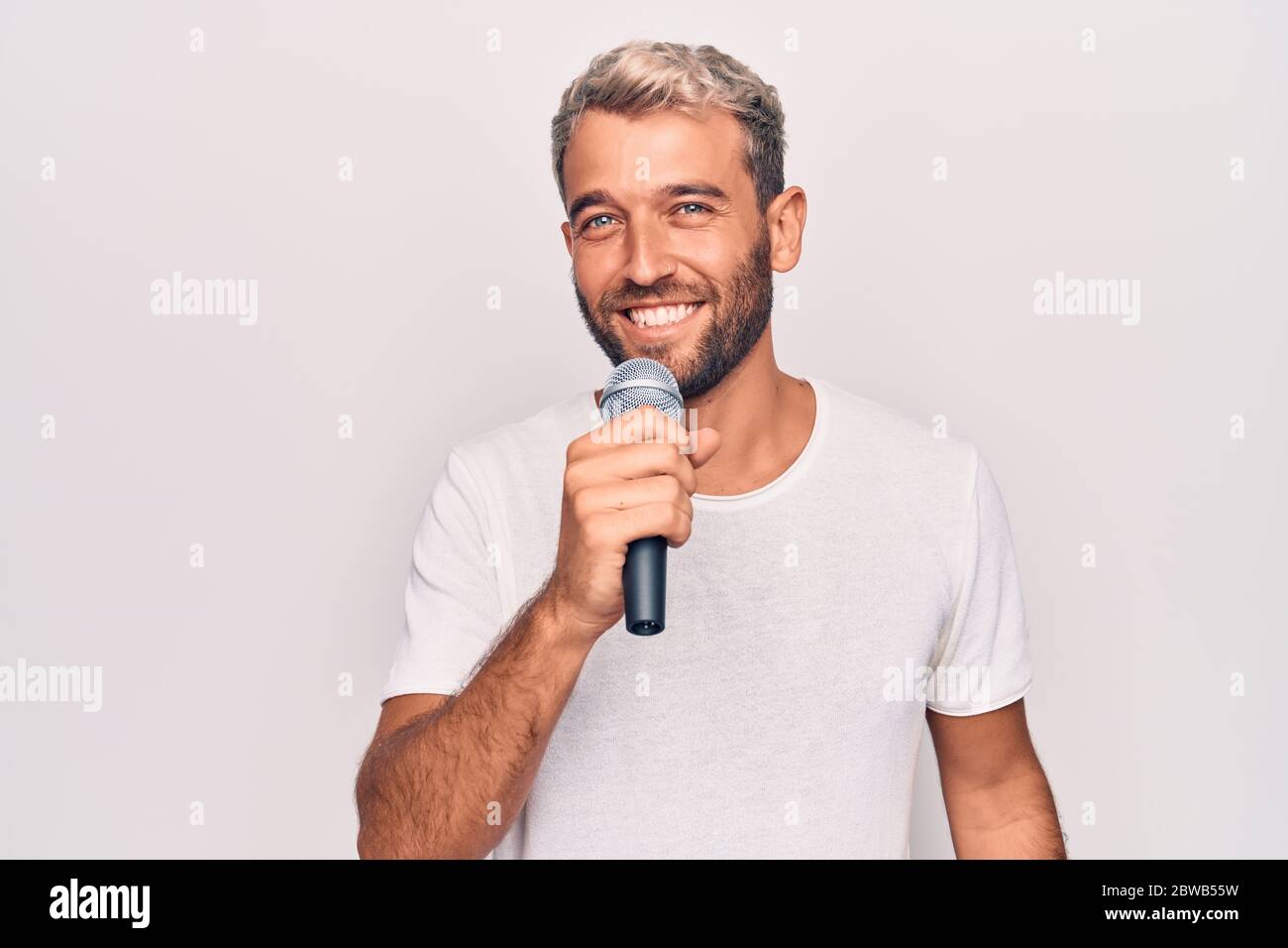 Handsome blond singer man with beard singing song using microphone over white background looking ...