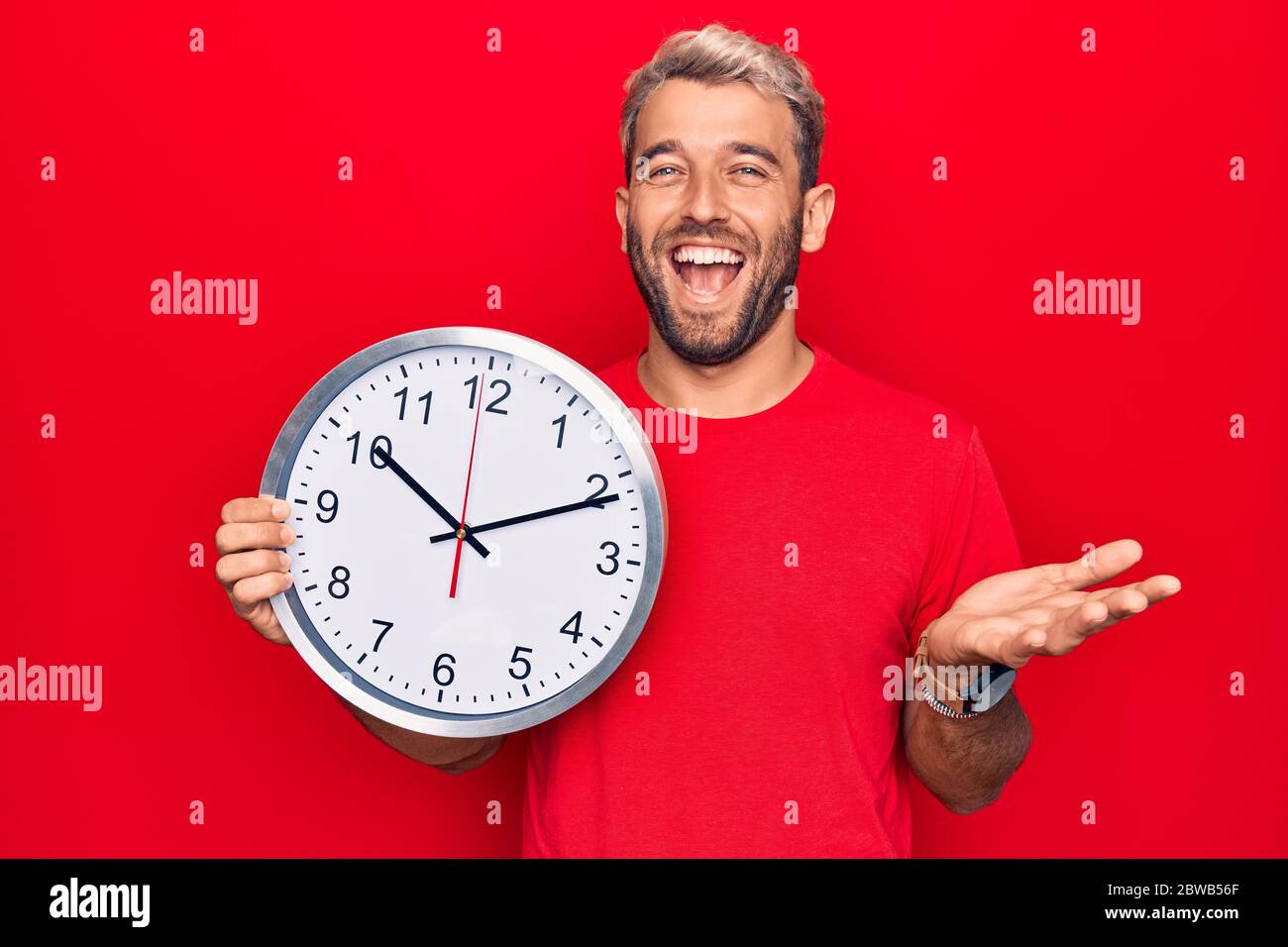 Young handsome blond man with beard doing countdown using big clock ...