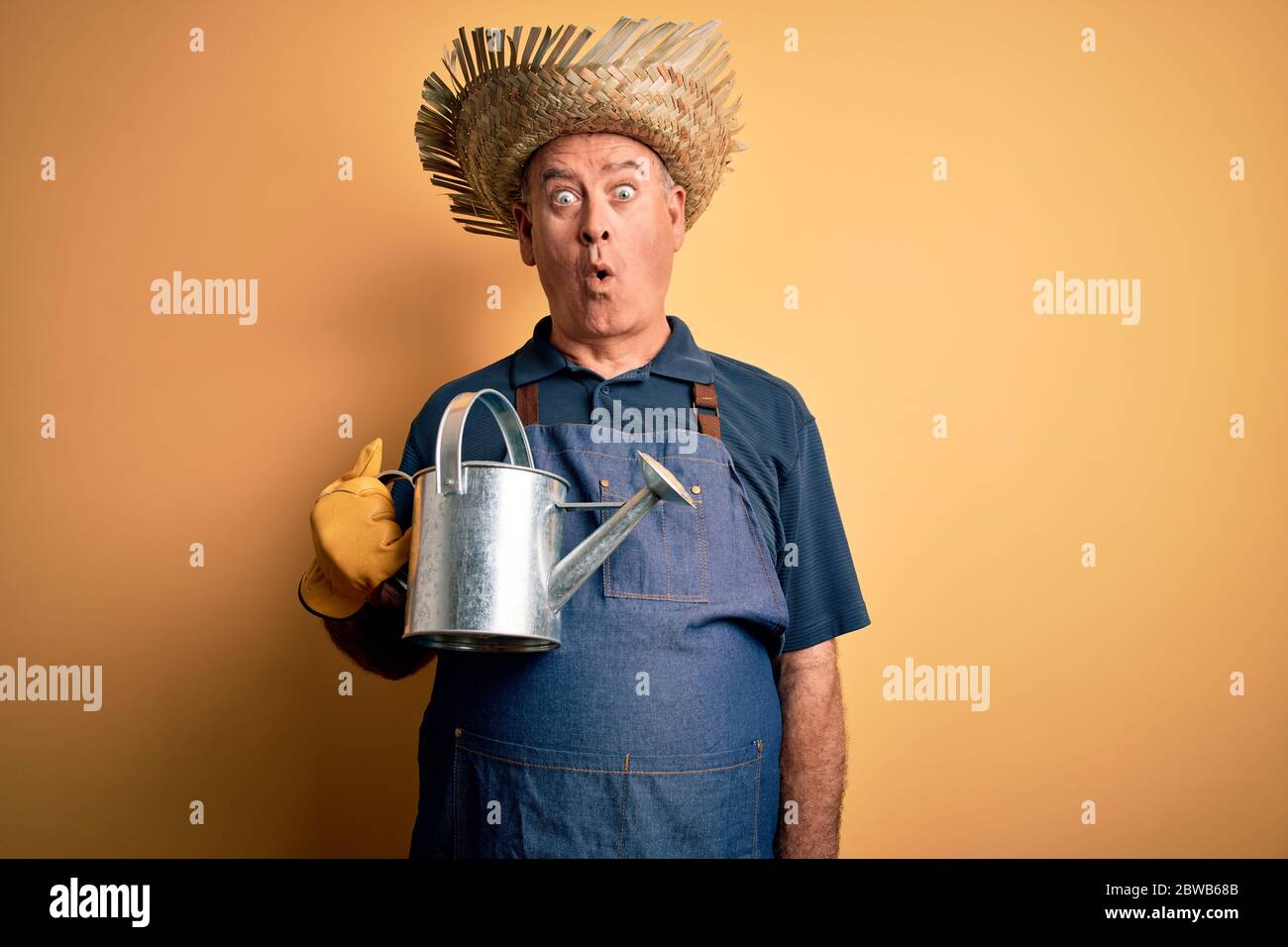Middle age farmer man wearing apron and hat holding watering can over ...
