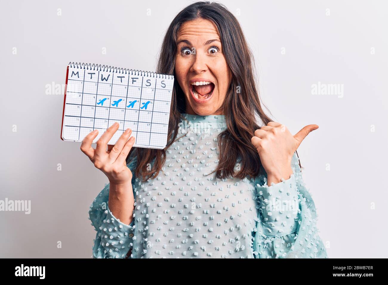 Young beautiful brunette woman holding travel calendar reminder over ...
