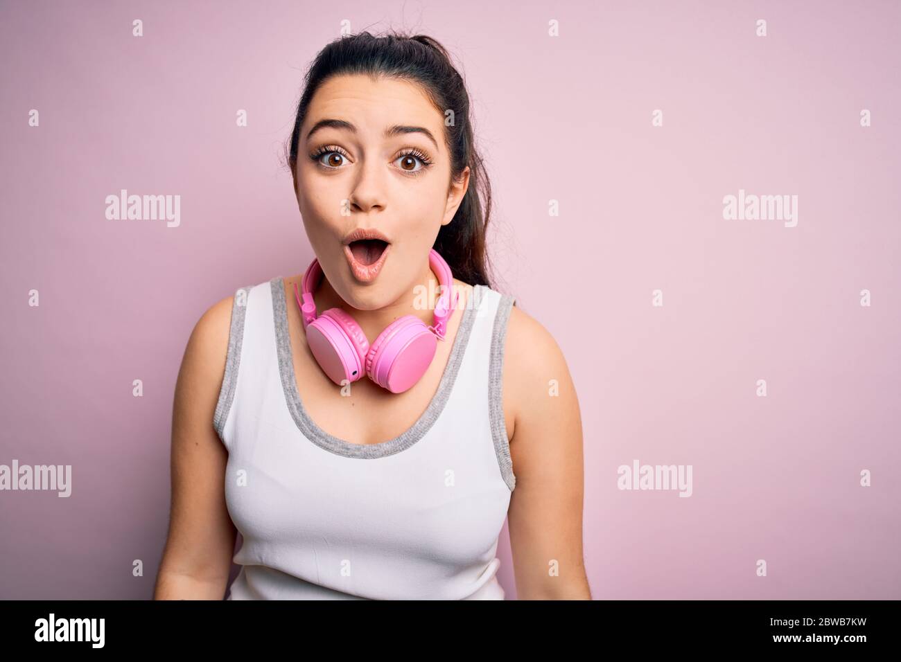 Young brunette fitness woman wearing gym headphones over pink isolated ...