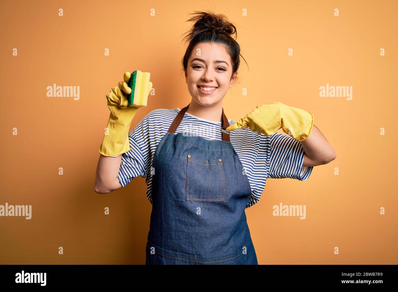 Young brunette cleaner woman wearing housekeeping gloves holding ...