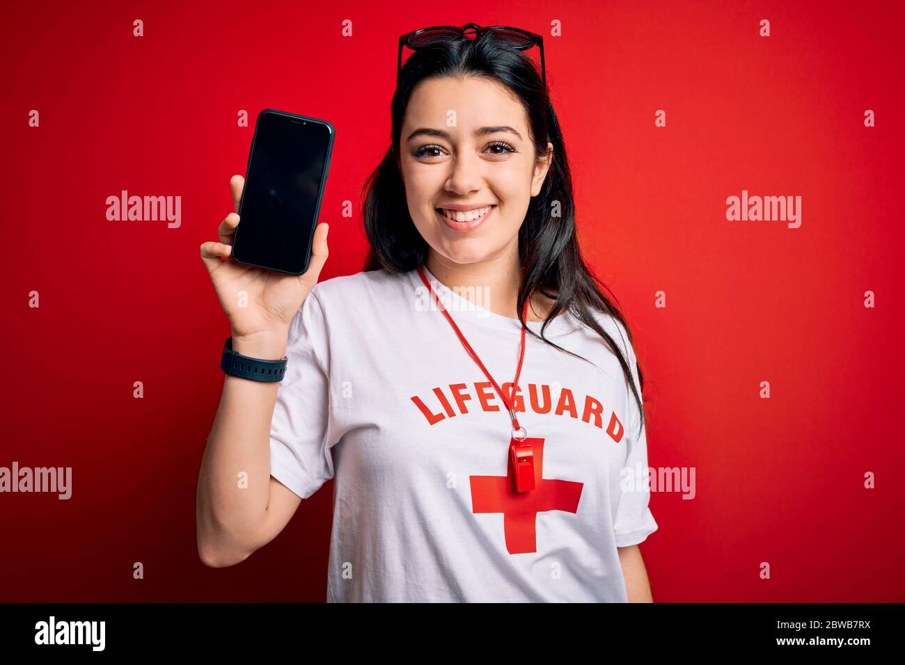 Young lifeguard woman showing smartphone screen over red background ...