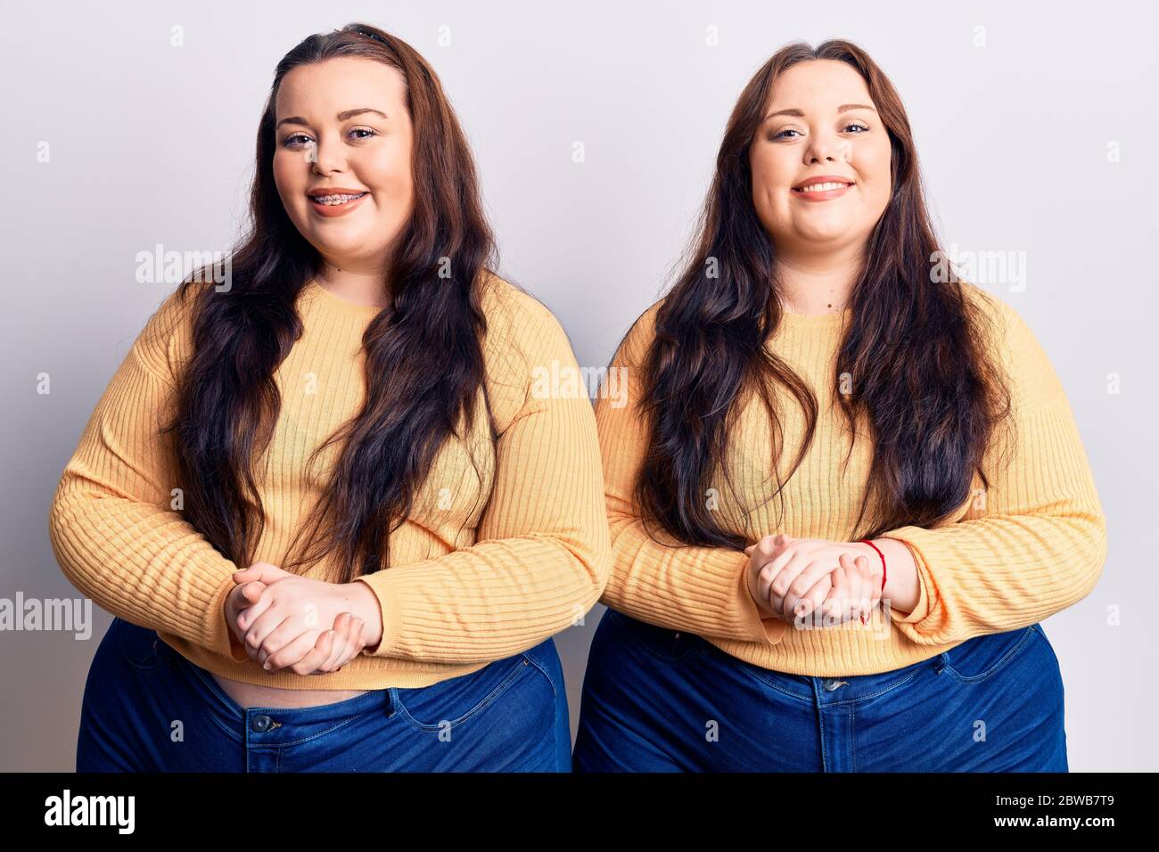 Young plus size twins wearing casual clothes with hands together and ...