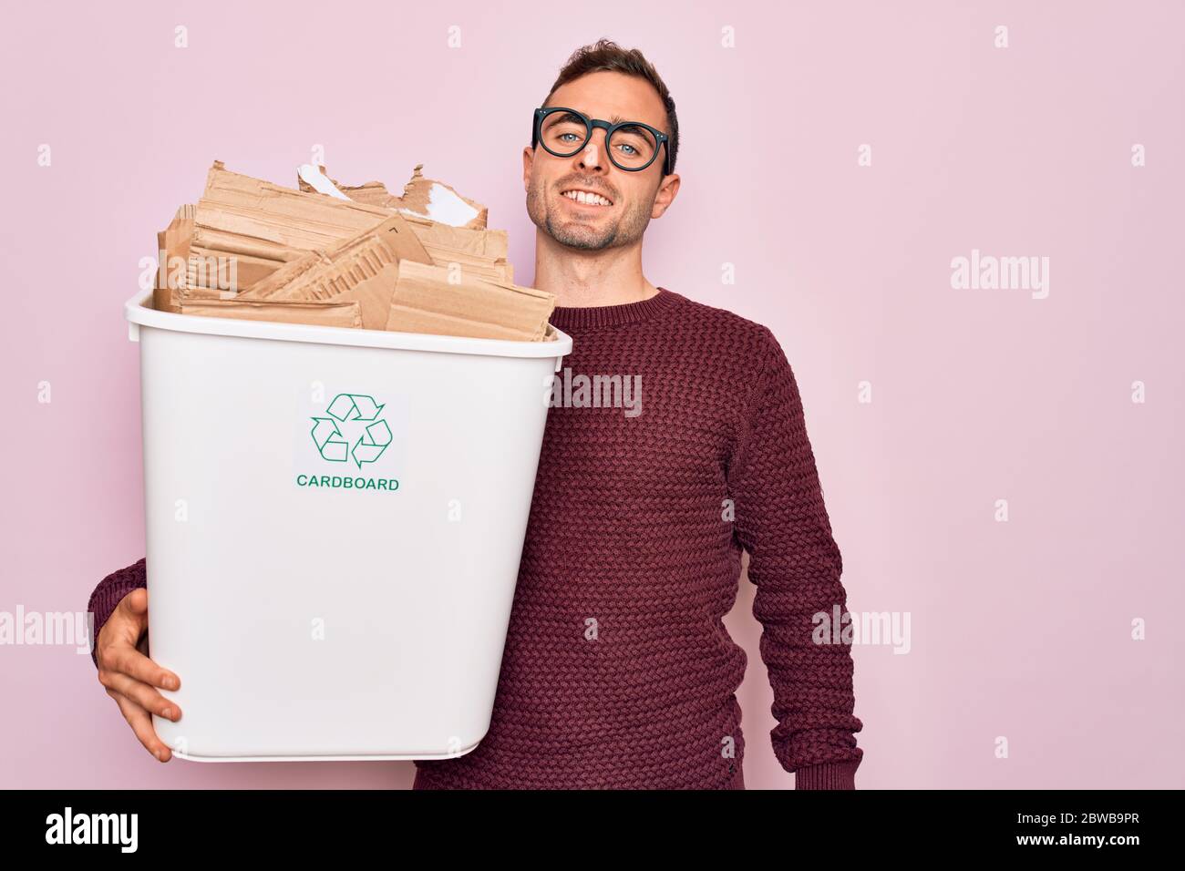Young handsome man with blue eyes recycling holding wastebasket with ...