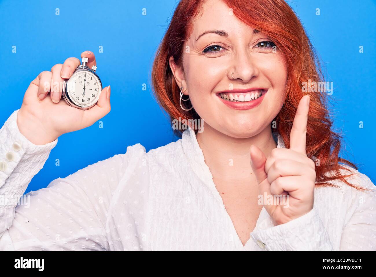 Young beautiful redhead woman doing countdown using stopwatch over blue ...