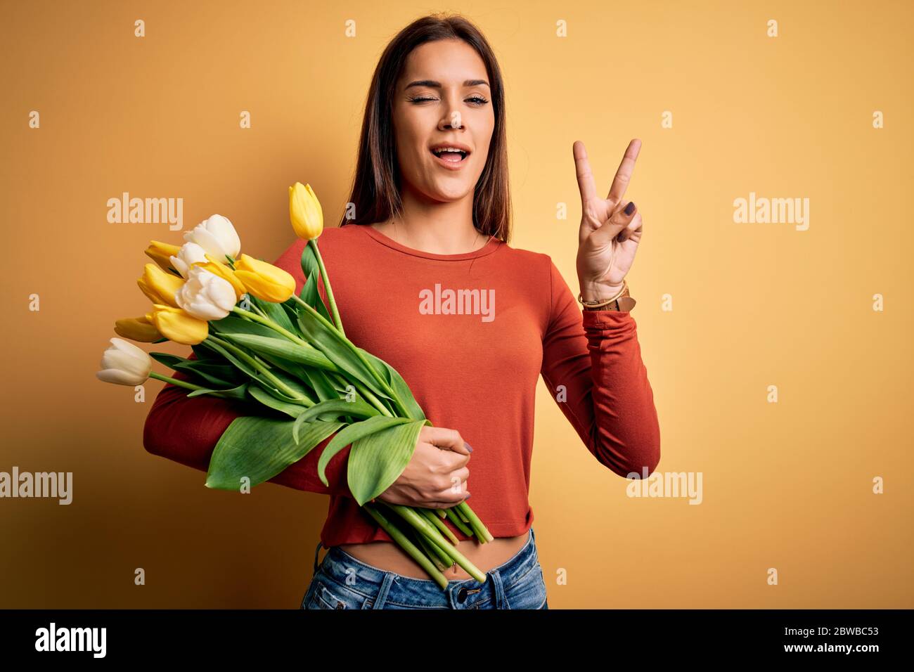 Young beautiful brunette woman holding bouquet of tulips flowers over ...