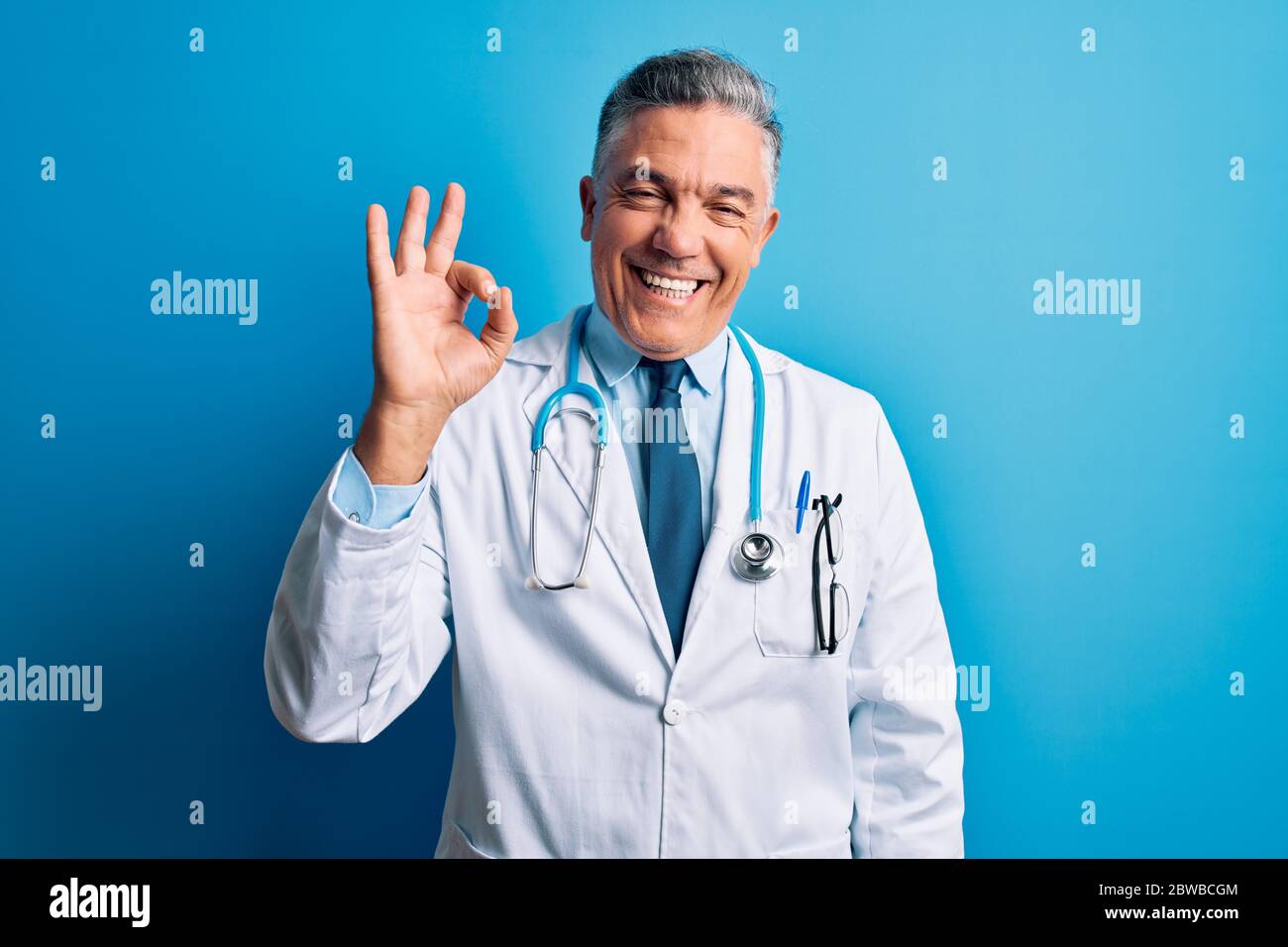 Middle age handsome grey-haired doctor man wearing coat and blue ...