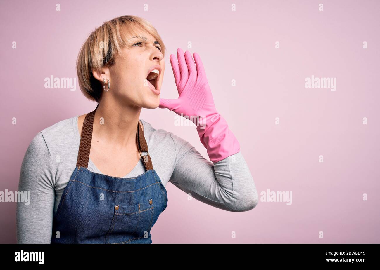 Young blonde cleaner woman with short hair wearing apron and gloves ...