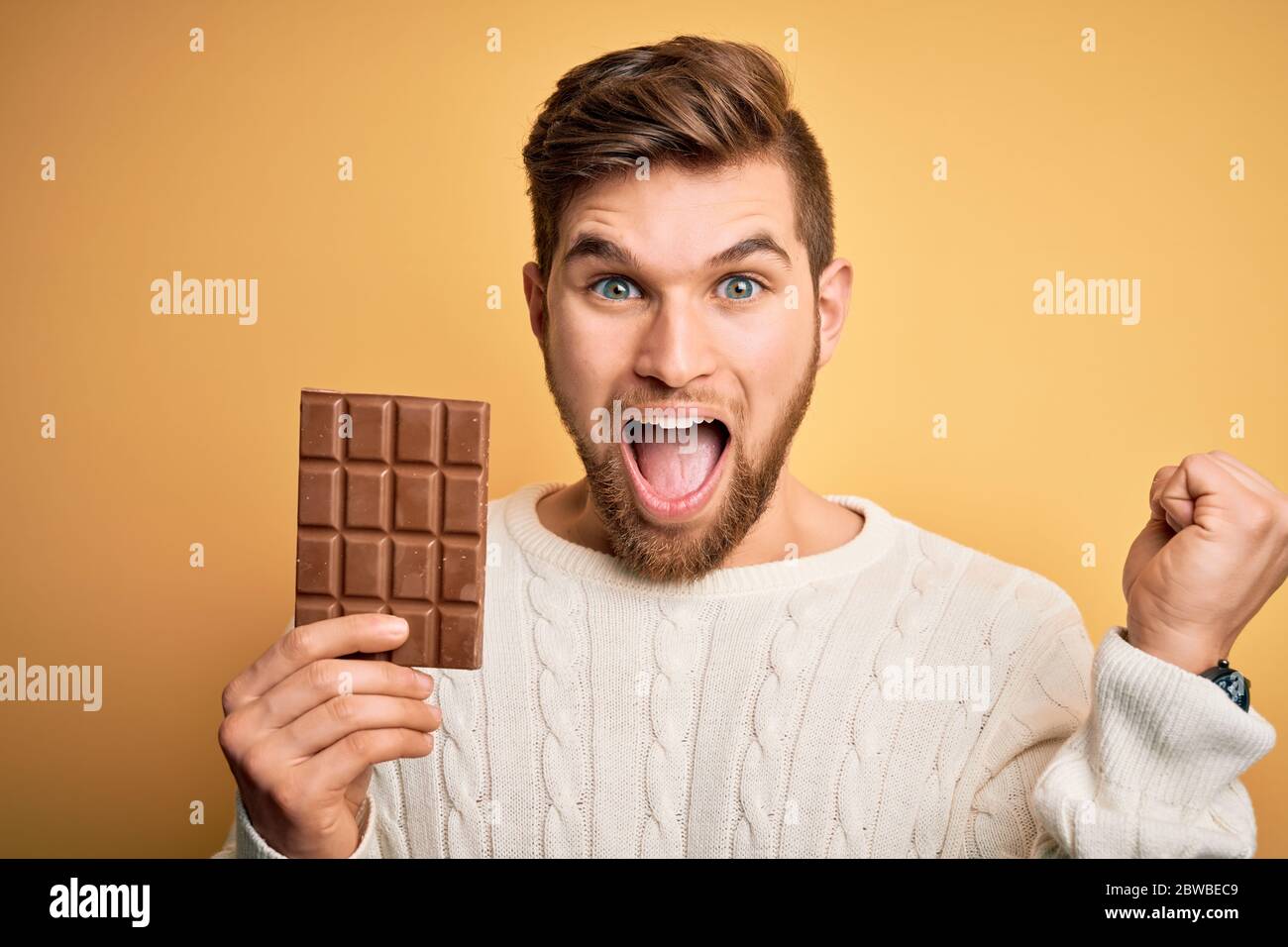 Young blond man with beard and blue eyes holding chocolate bar over ...