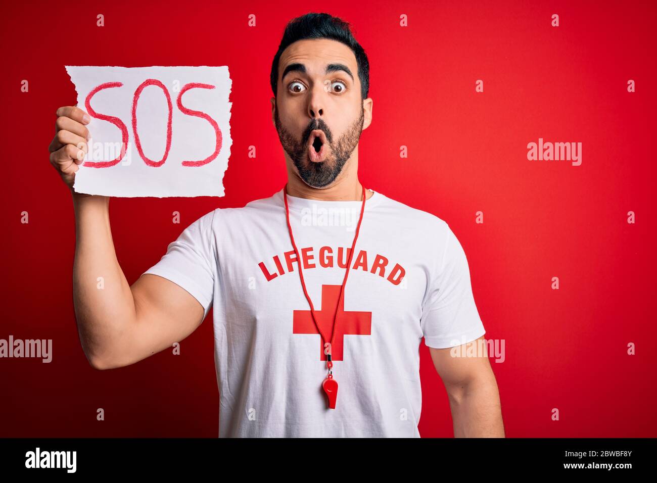 Young handsome lifeguard man with beard wearing whistle holding sos ...
