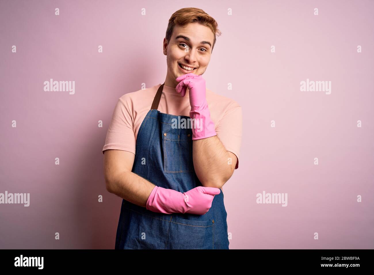 Young Handsome Redhead Cleaner Man Doing Housework Wearing Apron And Gloves Looking Confident At