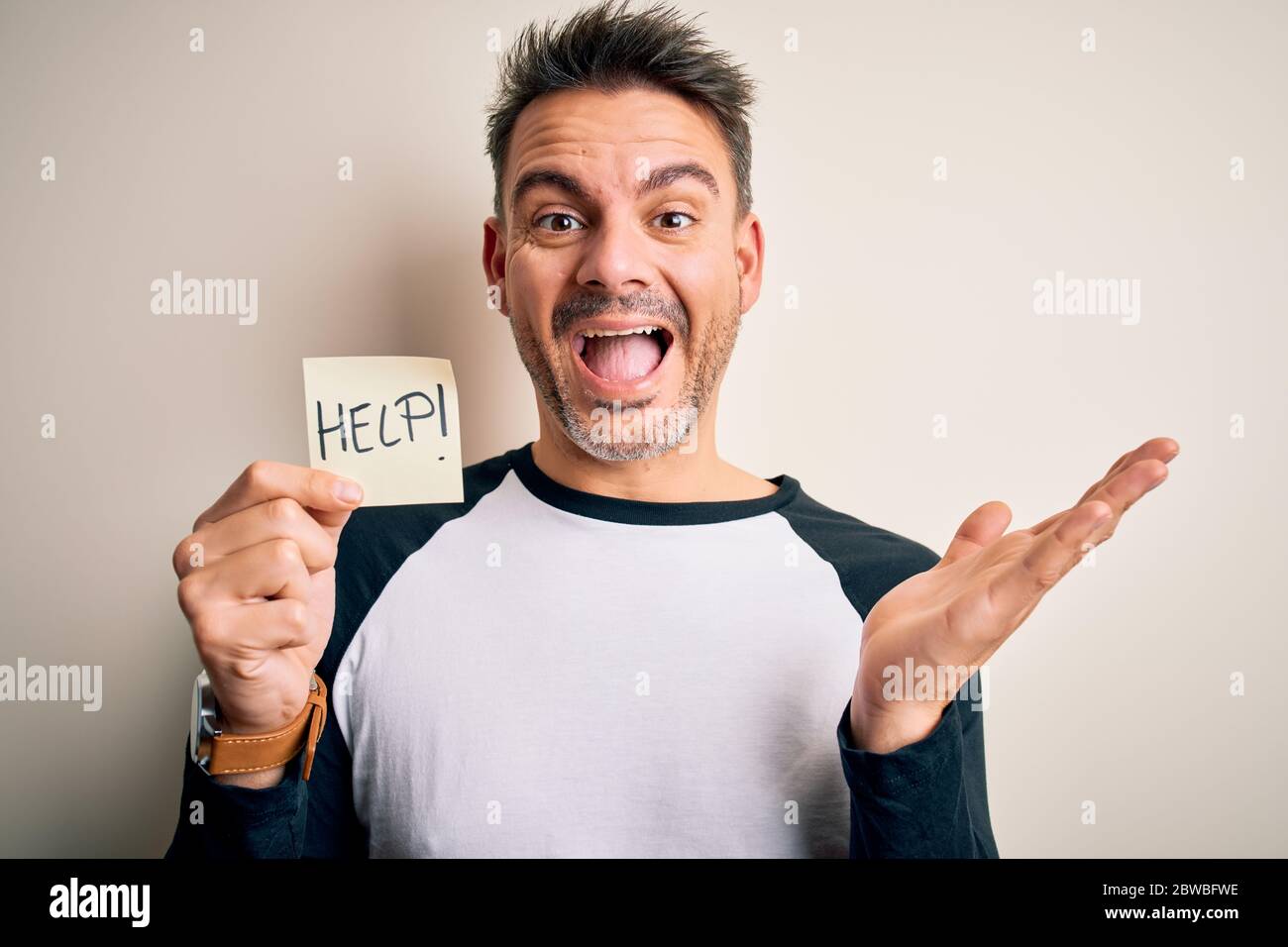 Young handsome man stressed holding reminder paper with help message ...