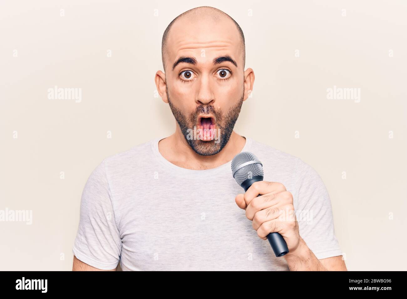 Young handsome bald man singing song using microphone scared and amazed ...