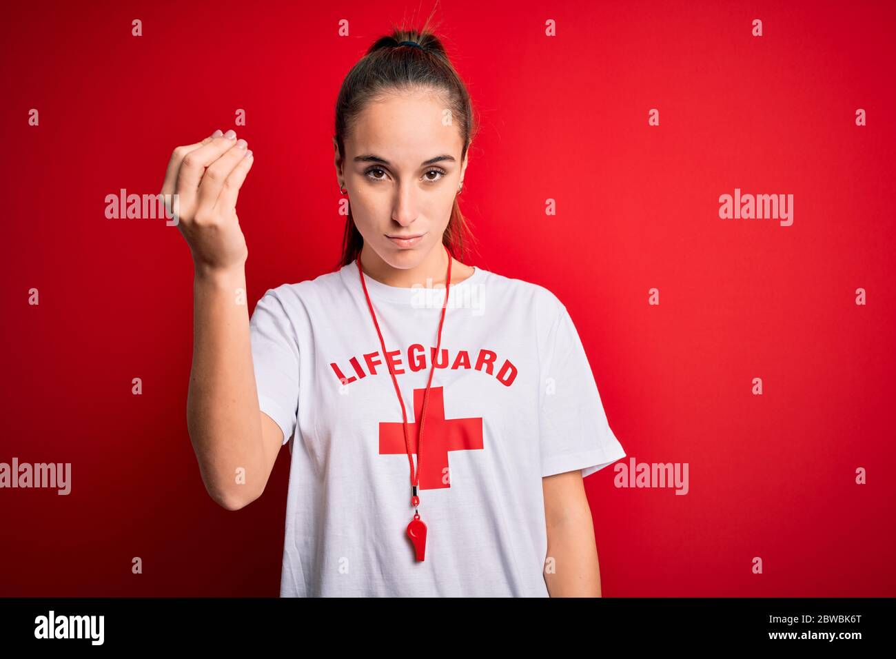 Beautiful lifeguard woman wearing t-shirt with red cross using whistle ...