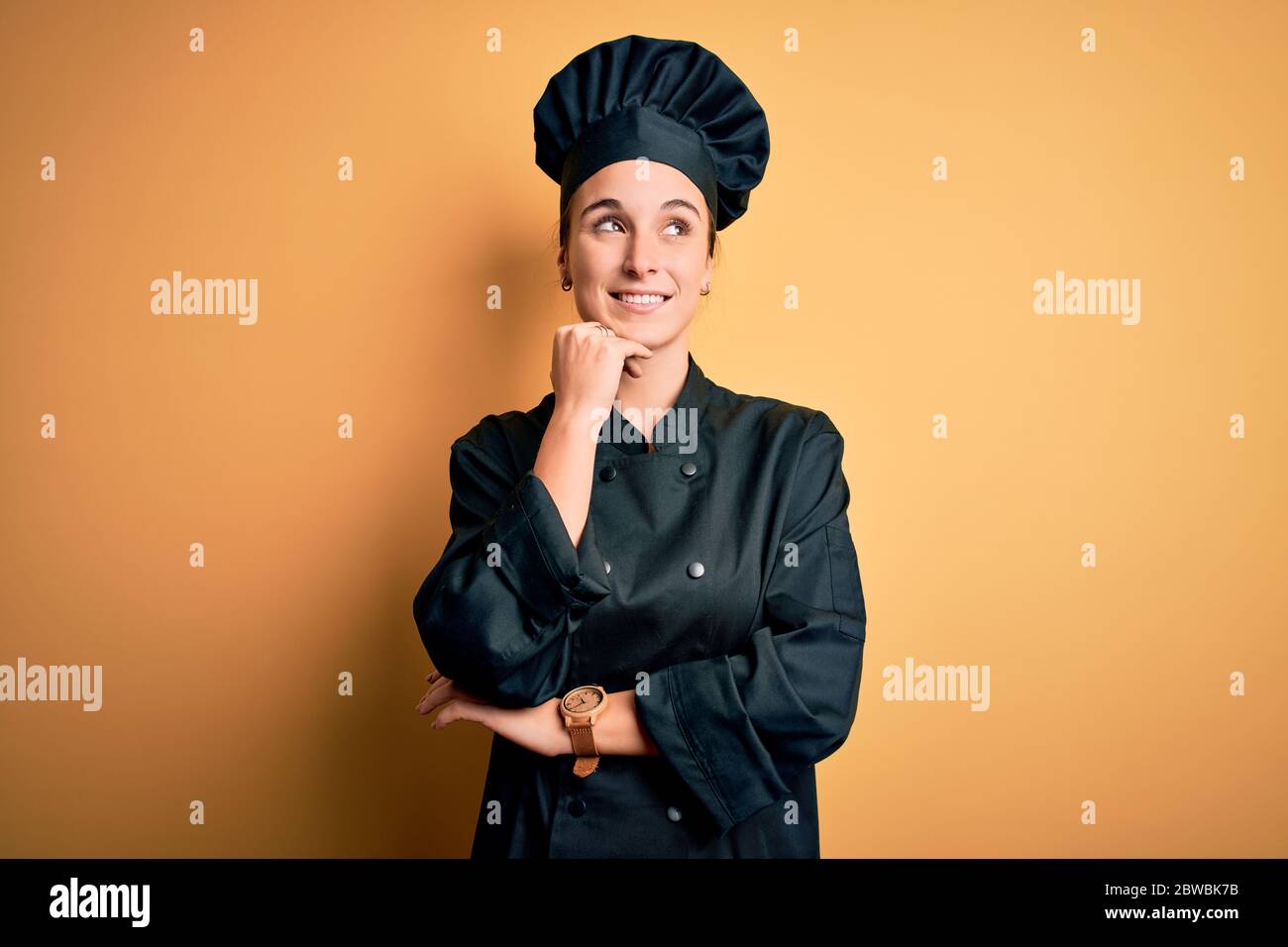 Young beautiful chef woman wearing cooker uniform and hat standing over ...