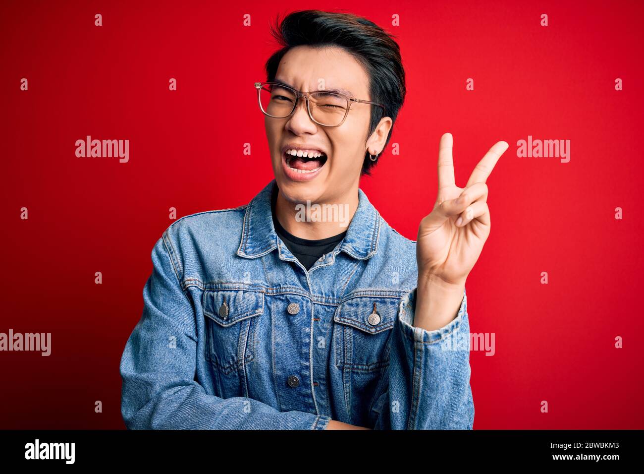 Young handsome chinese man wearing denim jacket and glasses over red ...