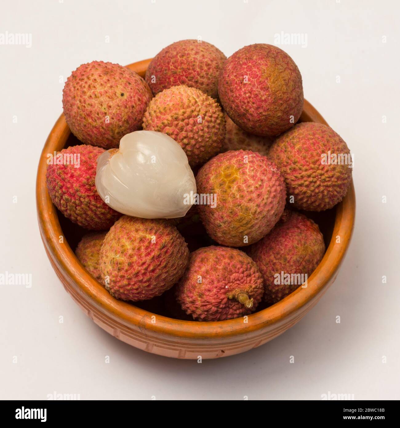 Close-up view of ripe lychee in an earthen bowl on white background ...