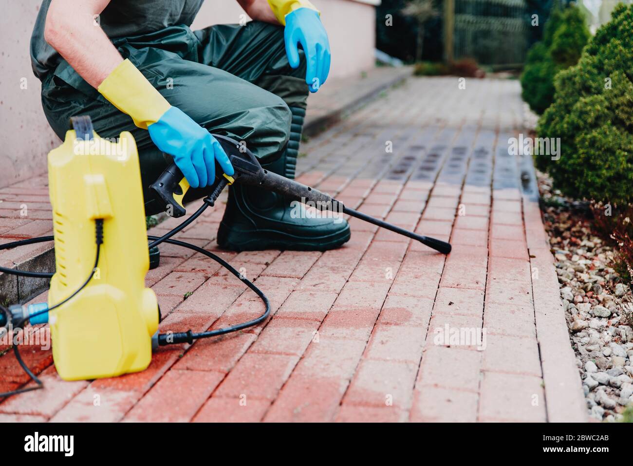 Man cleaning red, conrete pavement block using high pressure water ...