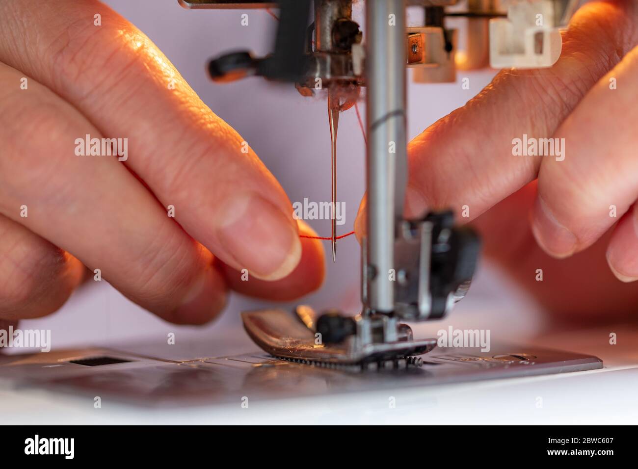 elder woman fingers inserting a red thread into a sewing machine's ...