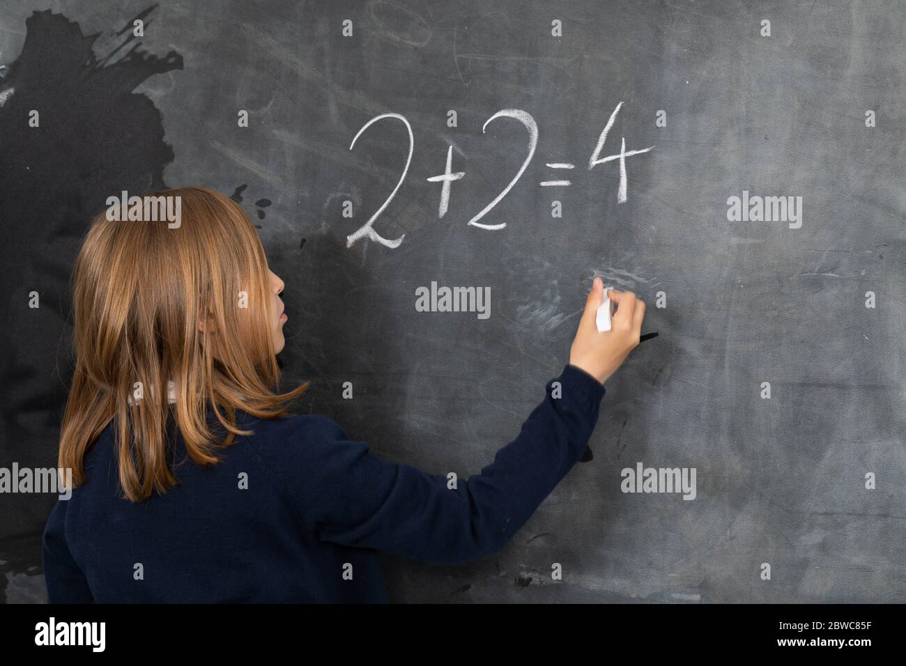 He writes on the chalkboard with chalk. Math problem. A girl at the ...