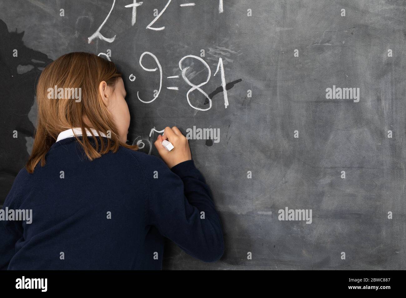 He writes on the chalkboard with chalk. Math problem. A girl at the ...