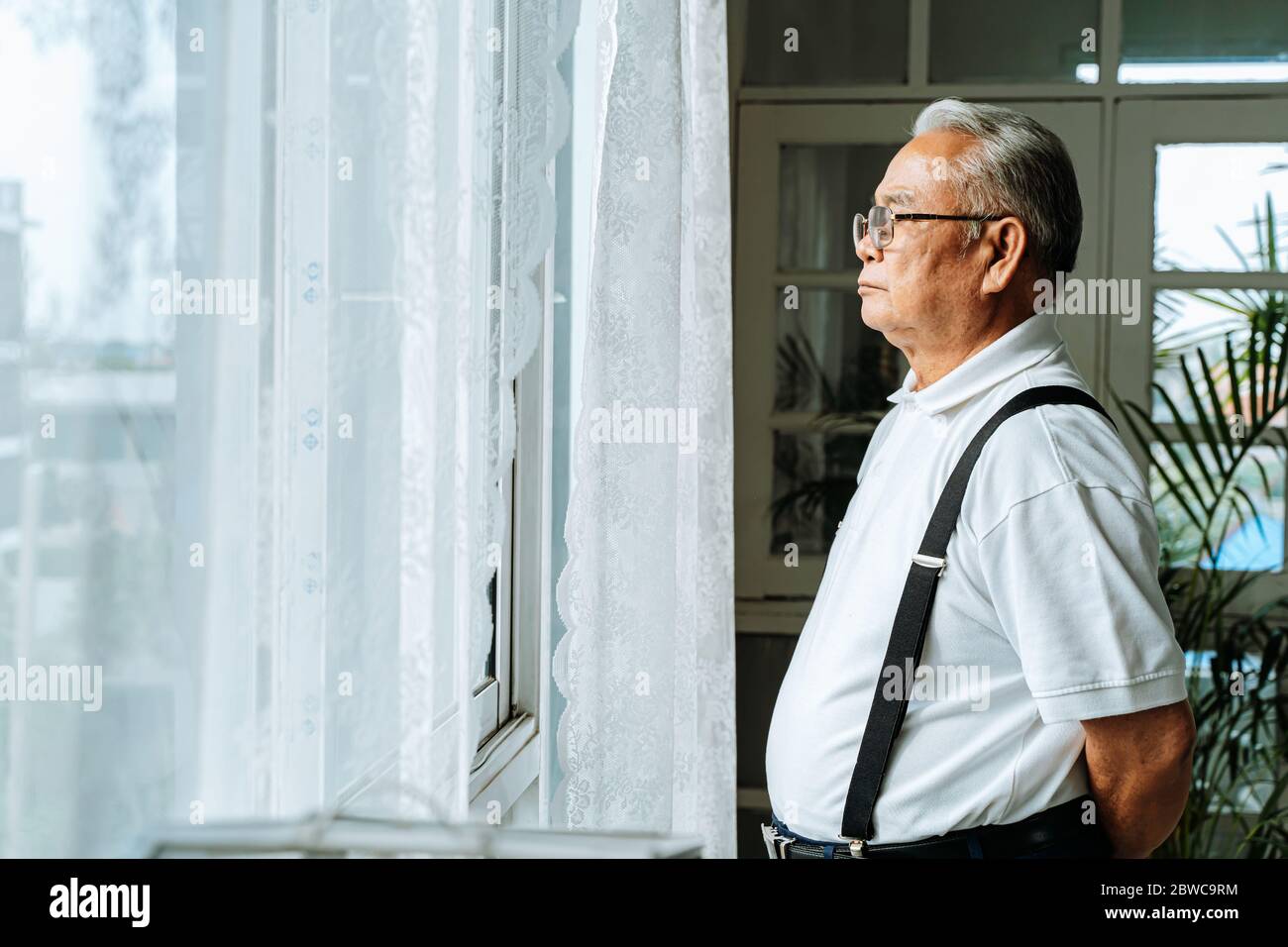 Close up of pensive old man with glasses looking out of window feeling ...