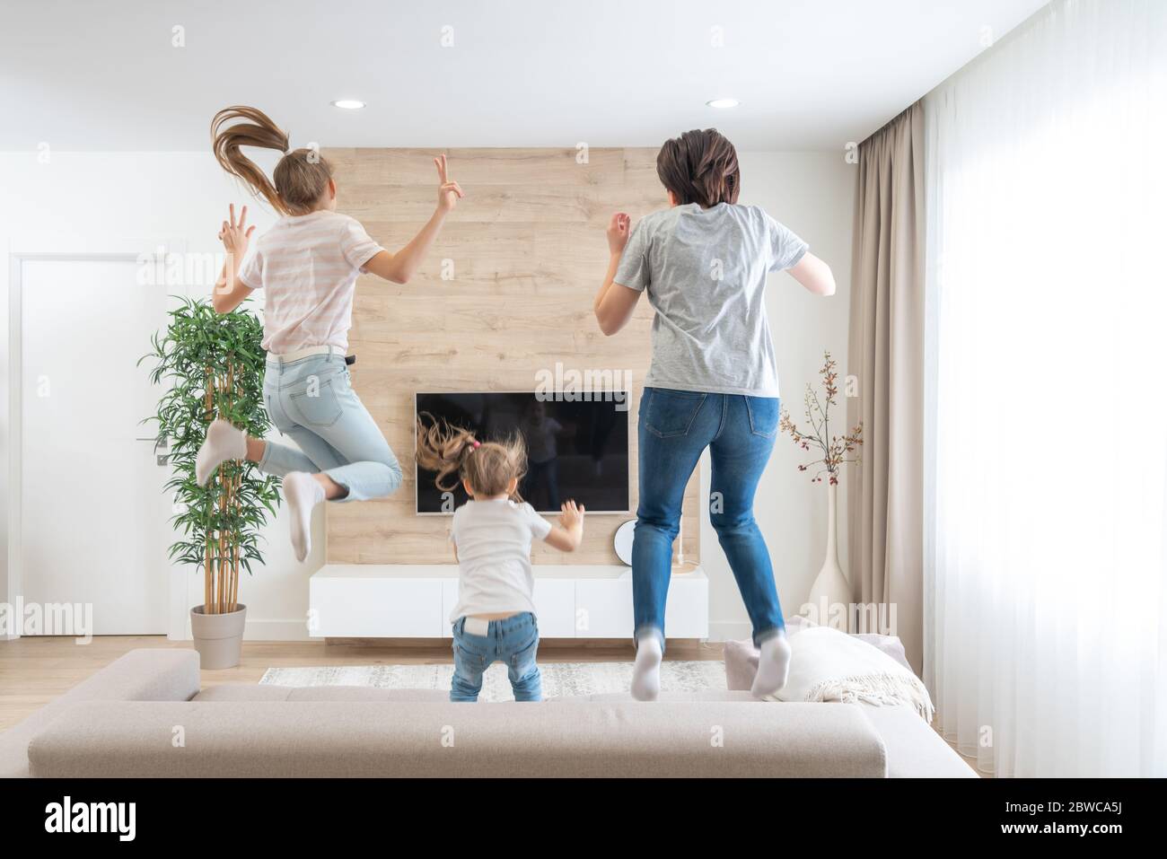 Mother and two daughters having fun jumping on a sofa in living room Stock Photo - Alamy