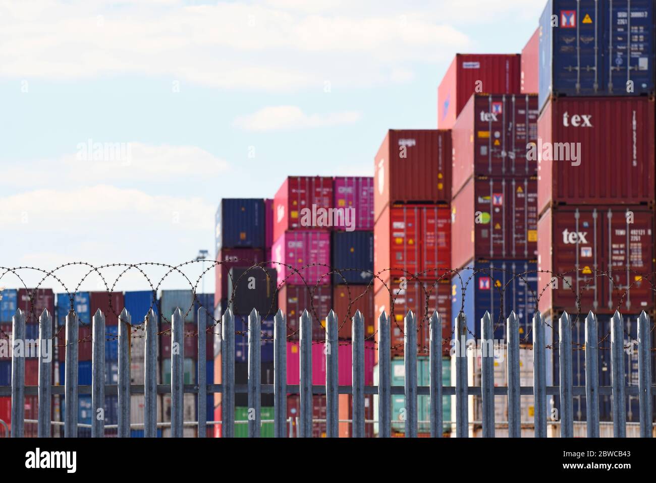 Freight shipping containers stacked behind a fence topped with barbed ...