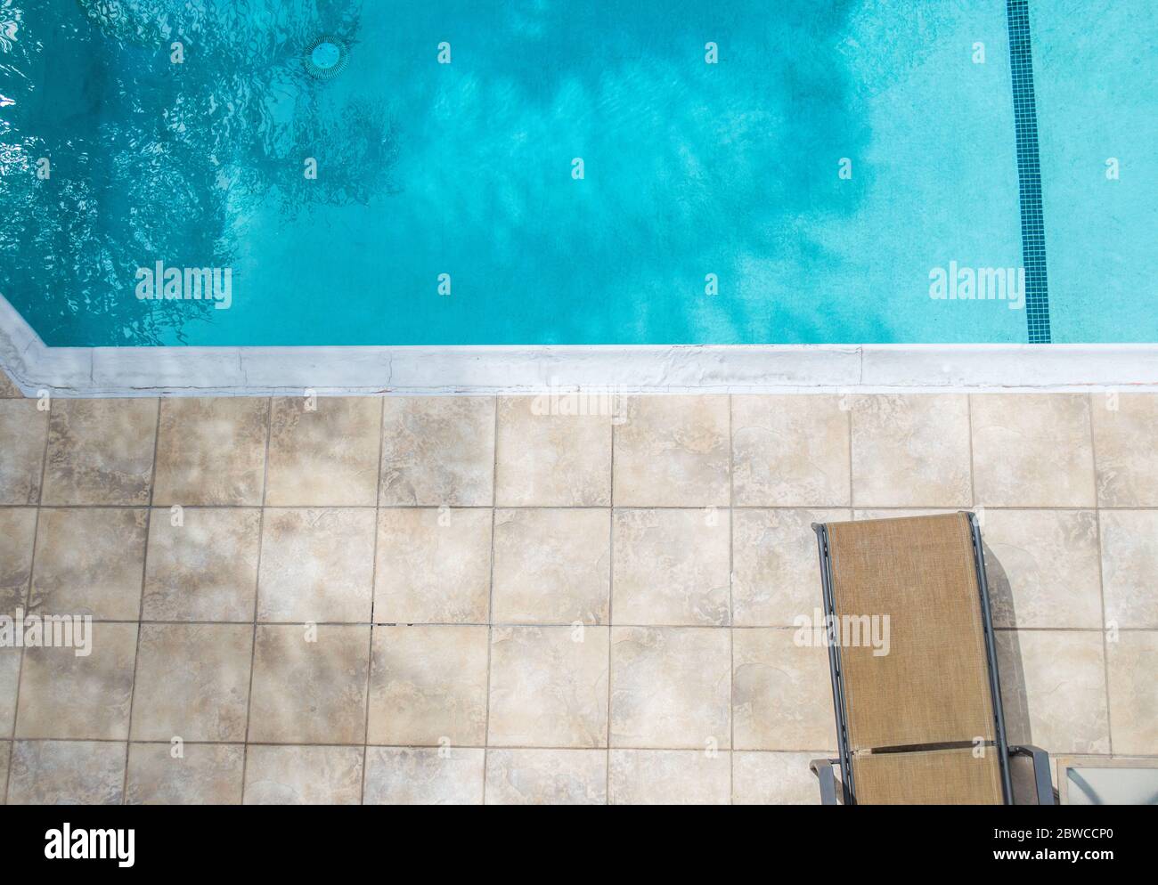 an empty swimming pool and tile pool deck with a brown chaise lounger ...