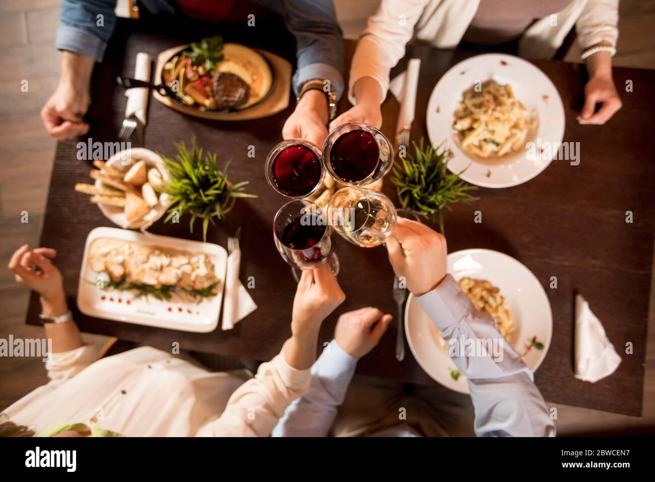 Four hands with red wine toasting over served table with food in the ...